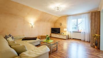 Sala de estar com sofá, mesa de centro de vidro, televisão e janela com cortinas.