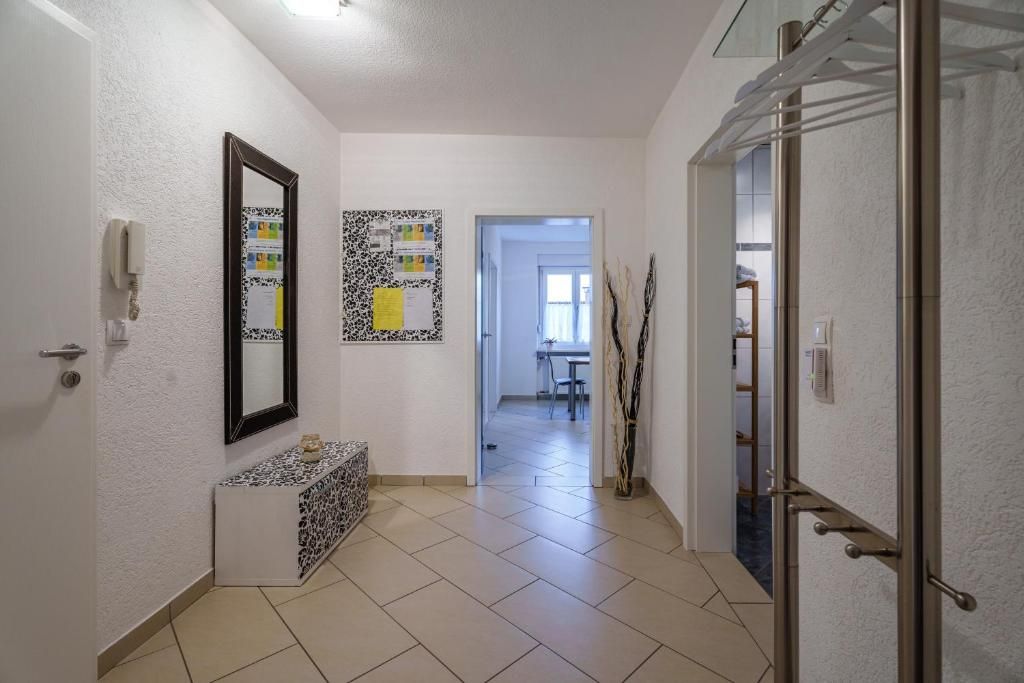 Um corredor com parede branca, espelho, quadro de avisos, banco e porta que dá para outro cômodo.