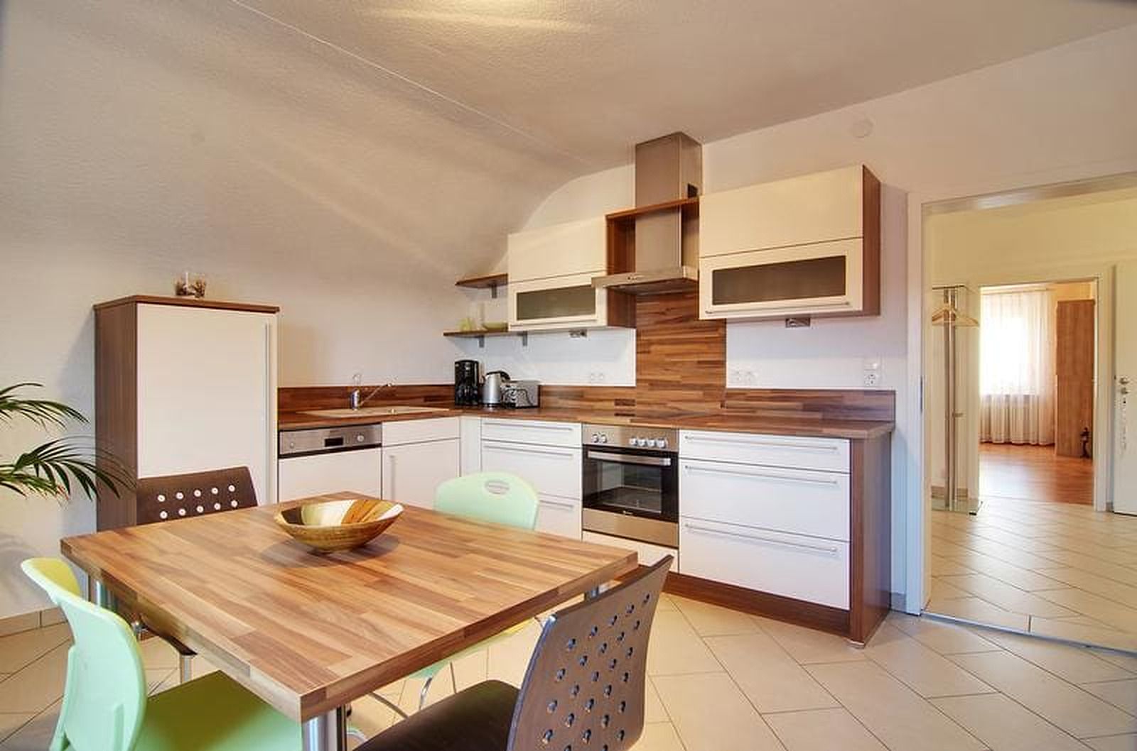Cozinha compacta com armários brancos, mesa de jantar de madeira e forno embutido.