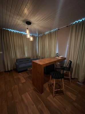 Espaço compacto com mesa de jantar de madeira, duas cadeiras, sofá e cozinha compacta.