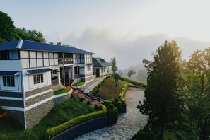 Um edifício de dois andares com uma varanda, uma parede de pedra e um caminho pavimentado que leva à entrada.