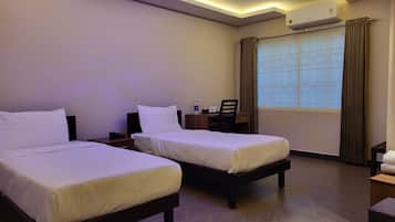 Quarto de hotel com duas camas, uma escrivaninha, uma cadeira, ar condicionado e uma janela com cortinas.