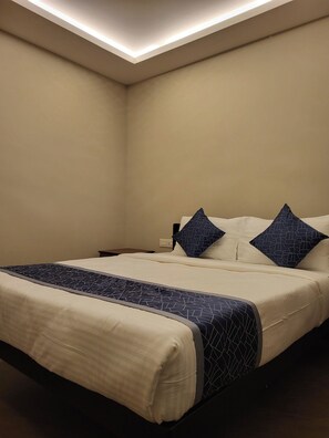 Quarto de hotel com cama, mesa de cabeceira e iluminação no teto.