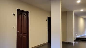 Um corredor com porta de madeira, luminárias embutidas no teto e piso ladrilhado.