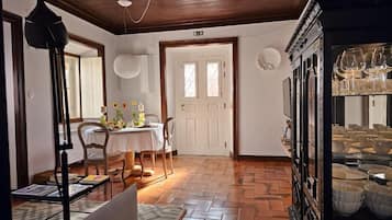 Quarto com piso de madeira, uma mesa de jantar com cadeiras, uma porta branca e um armário com copos.