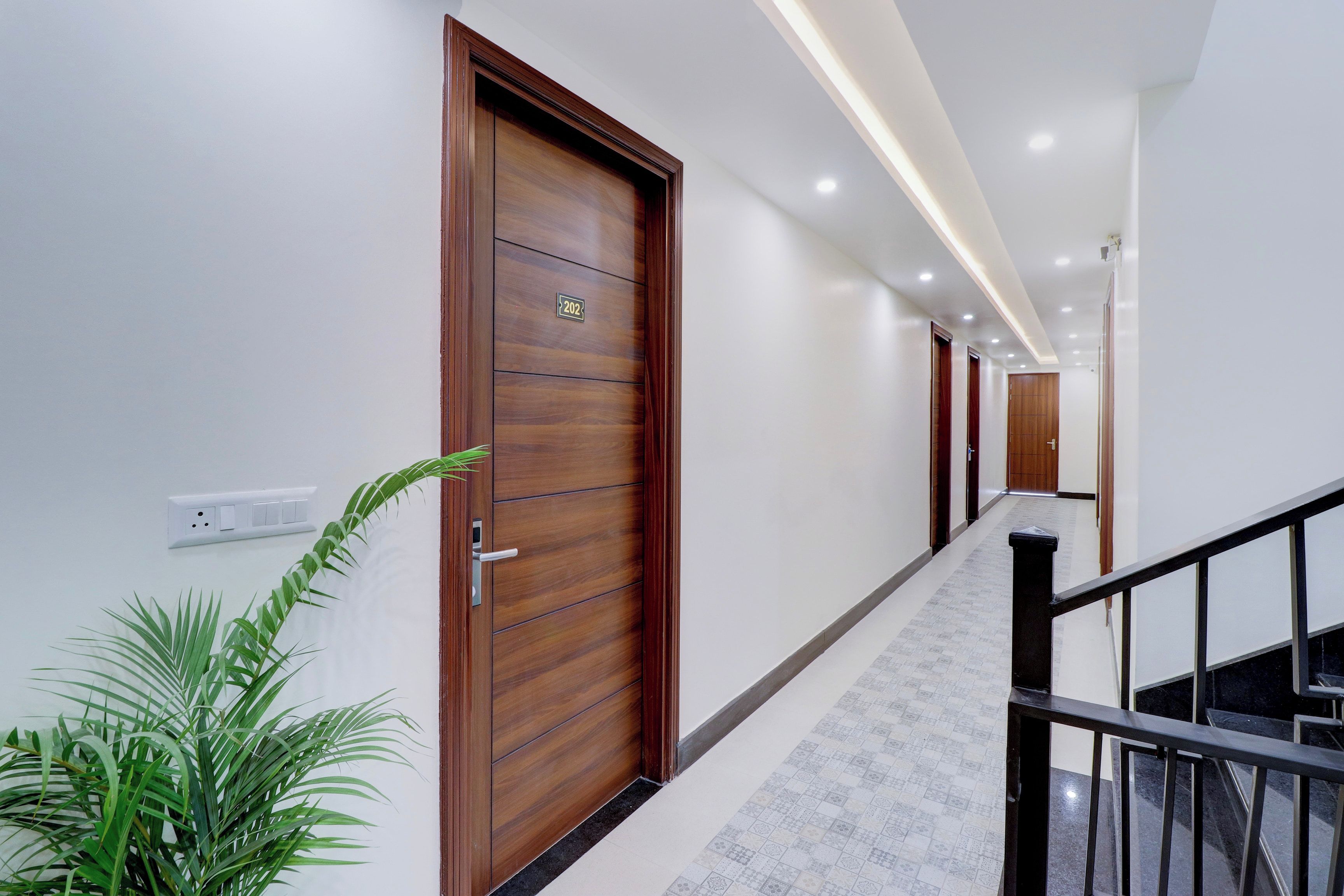 Corredor de hotel com portas de madeira, escada e planta em vaso.