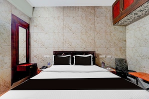 Quarto de hotel com parede estampada em mármore, uma cama grande com roupa de cama preta e branca, uma mesa de cabeceira de madeira, uma escrivaninha e uma cadeira.