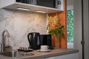 Cozinha moderna com bancada de mármore, chaleira, cafeteira, xícara e vaso com plantas verdes.