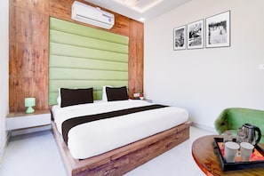 Quarto de hotel com uma cama, cabeceira estofada em verde, ar condicionado fixado na parede e quadros emoldurados.
