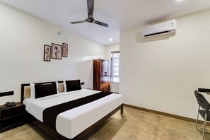 Quarto de hotel com cama, mesa de cabeceira e escrivaninha com cadeira.