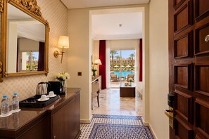 Um saguão de hotel com balcão de recepção, um espelho grande, vista para área de piscina externa e piso estampado.