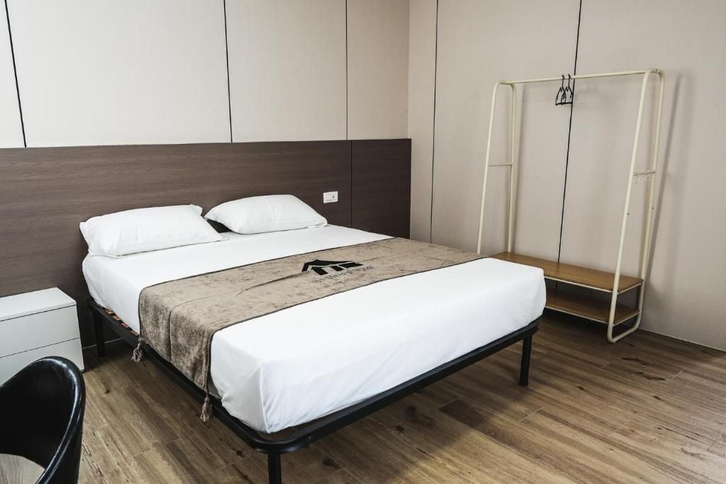 Uma cama de solteiro com cabeceira de madeira, uma mesa de cabeceira e uma cadeira branca.