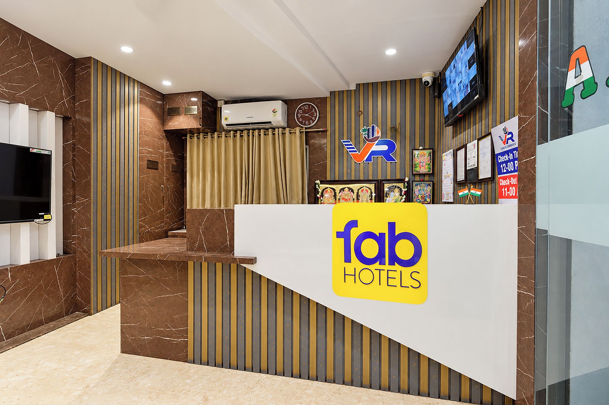 Área de recepção de hotel com balcão de mármore, televisão e placa com o nome 'fab hotels'.