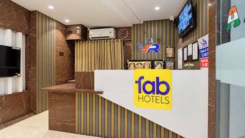 Área de recepção de hotel com balcão de mármore, televisão e placa com o nome 'fab hotels'.