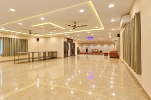 Um hall de hotel espaçoso com piso de mármore polido, ventiladores de teto, iluminação embutida e uma área de estar com sofás e mesa de centro.