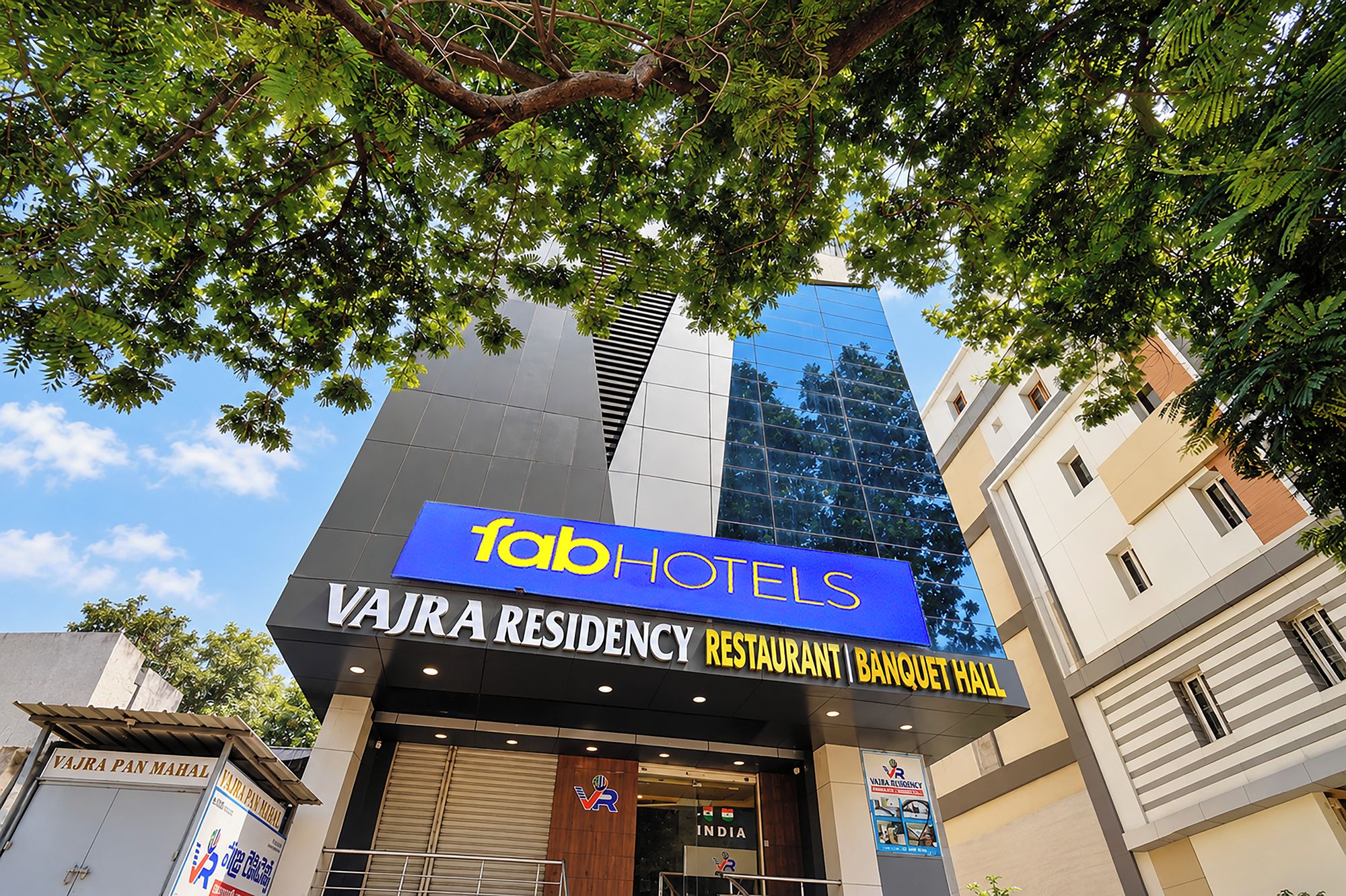 Fachada de hotel com placa indicando 'fahotels' e 'Vajra Residency Restaurant | Salão de Festas'.