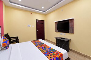 Quarto de hotel com cama, escrivaninha, televisão na parede e porta.