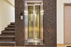 Um elevador com visor digital, ladeado por uma escada e uma porta com design geométrico.