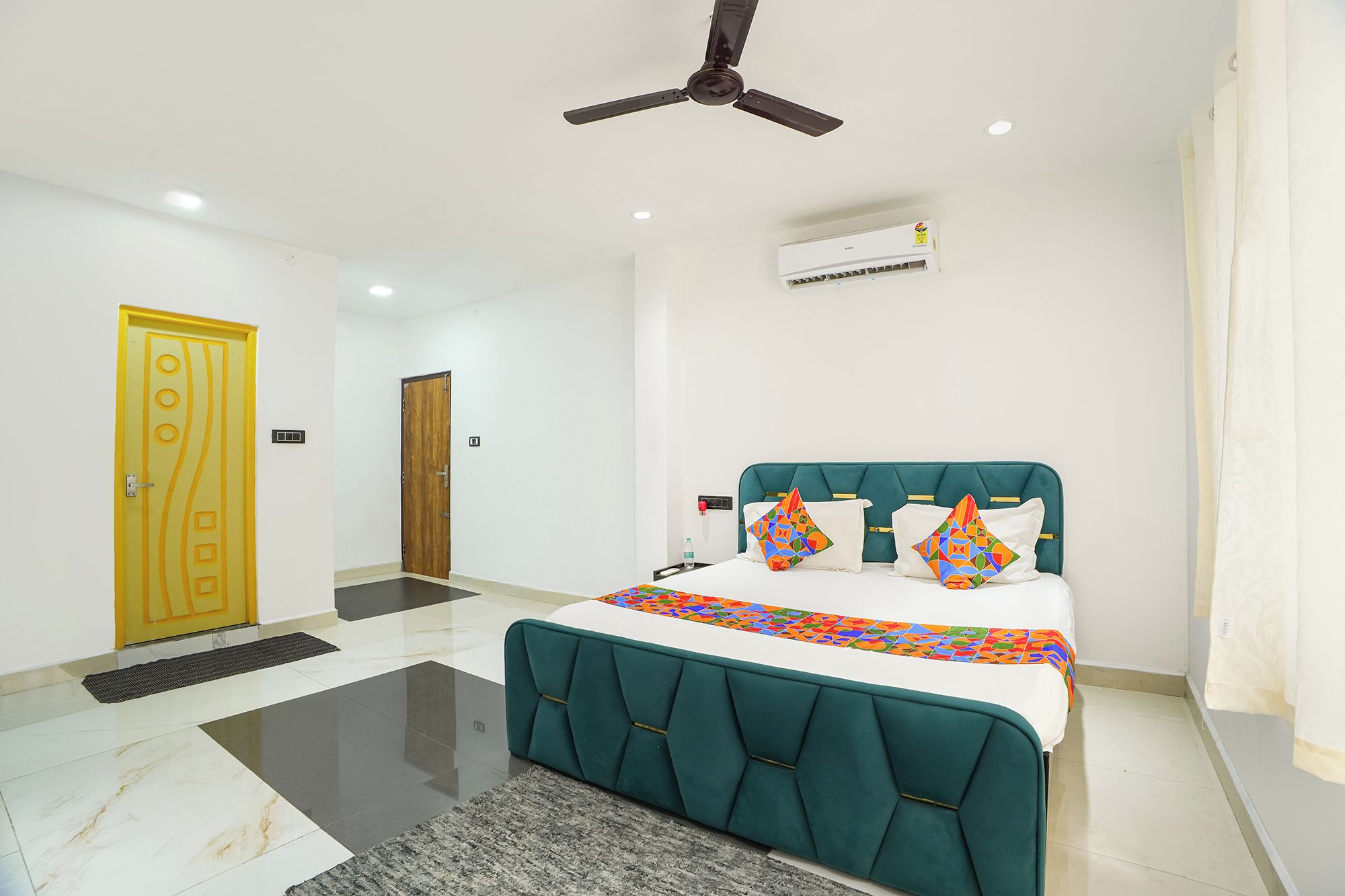Quarto de hotel com cama, ventoinha no teto, ar condicionado e porta amarela.