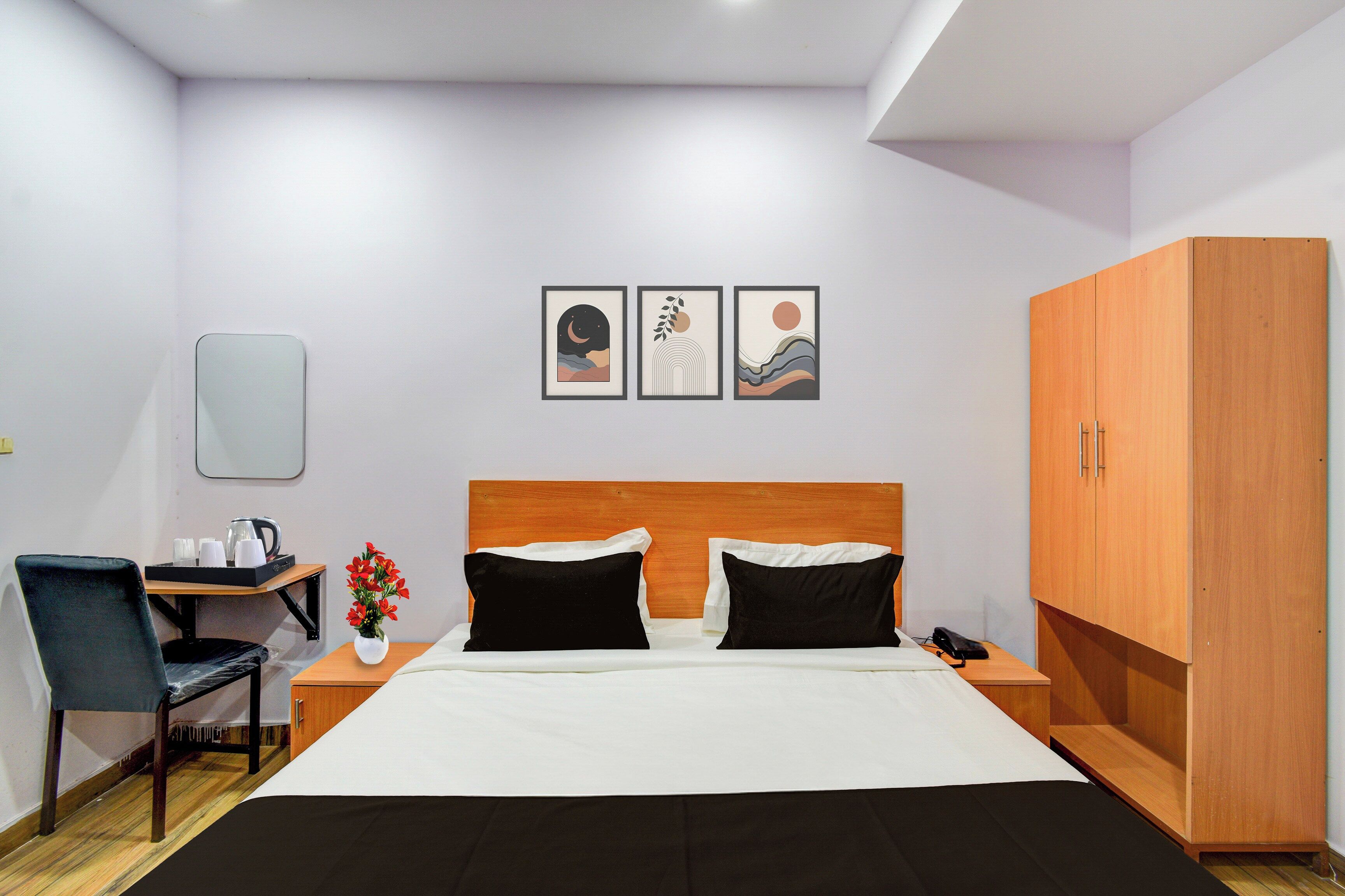 Quarto de hotel com uma cama, uma escrivaninha com cadeira, um guarda-roupa e três quadros na parede.