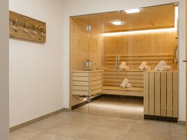Sala de sauna com bancos de madeira, porta de vidro e toalhas sobre um balcão.