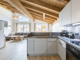Cozinha moderna com armários brancos, teto de madeira e lava-louças embutida.