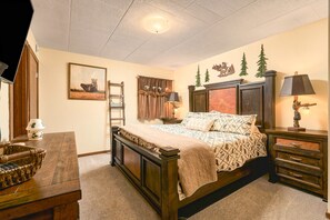 Quarto com cama de madeira, mesa de cabeceira com abajur, cômoda, cadeira, quadro na parede e luminária no teto.