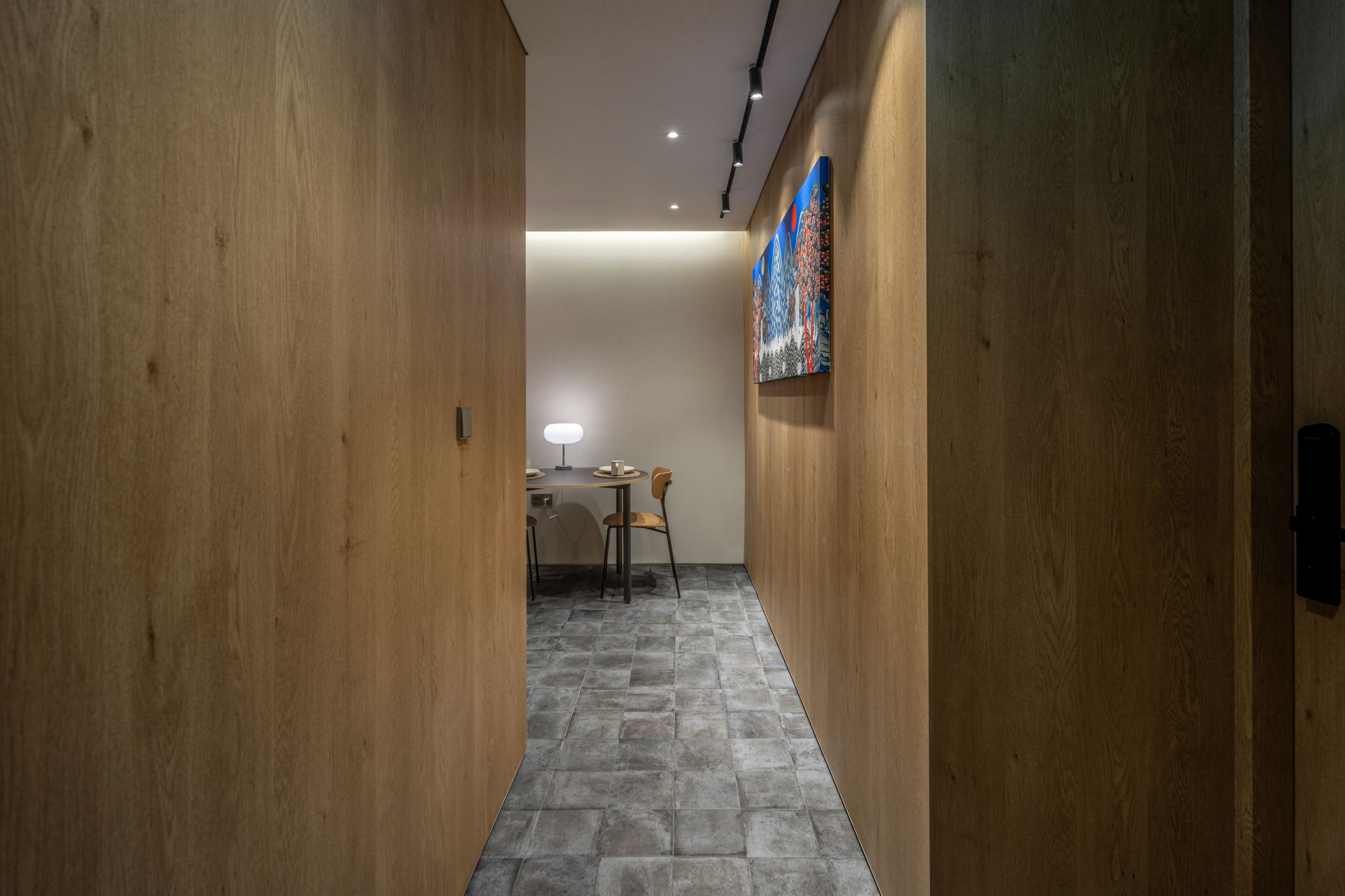 Corredor com paredes de madeira e piso de azulejos, que leva a uma sala de jantar com mesa e cadeiras.