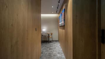 Corredor com paredes de madeira e piso de azulejos, que leva a uma sala de jantar com mesa e cadeiras.