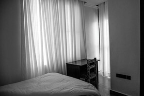 Quarto com cama, escrivaninha e cortinas.