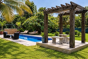 Área de piscina com pergolado, espreguiçadeiras e uma pequena mesa.