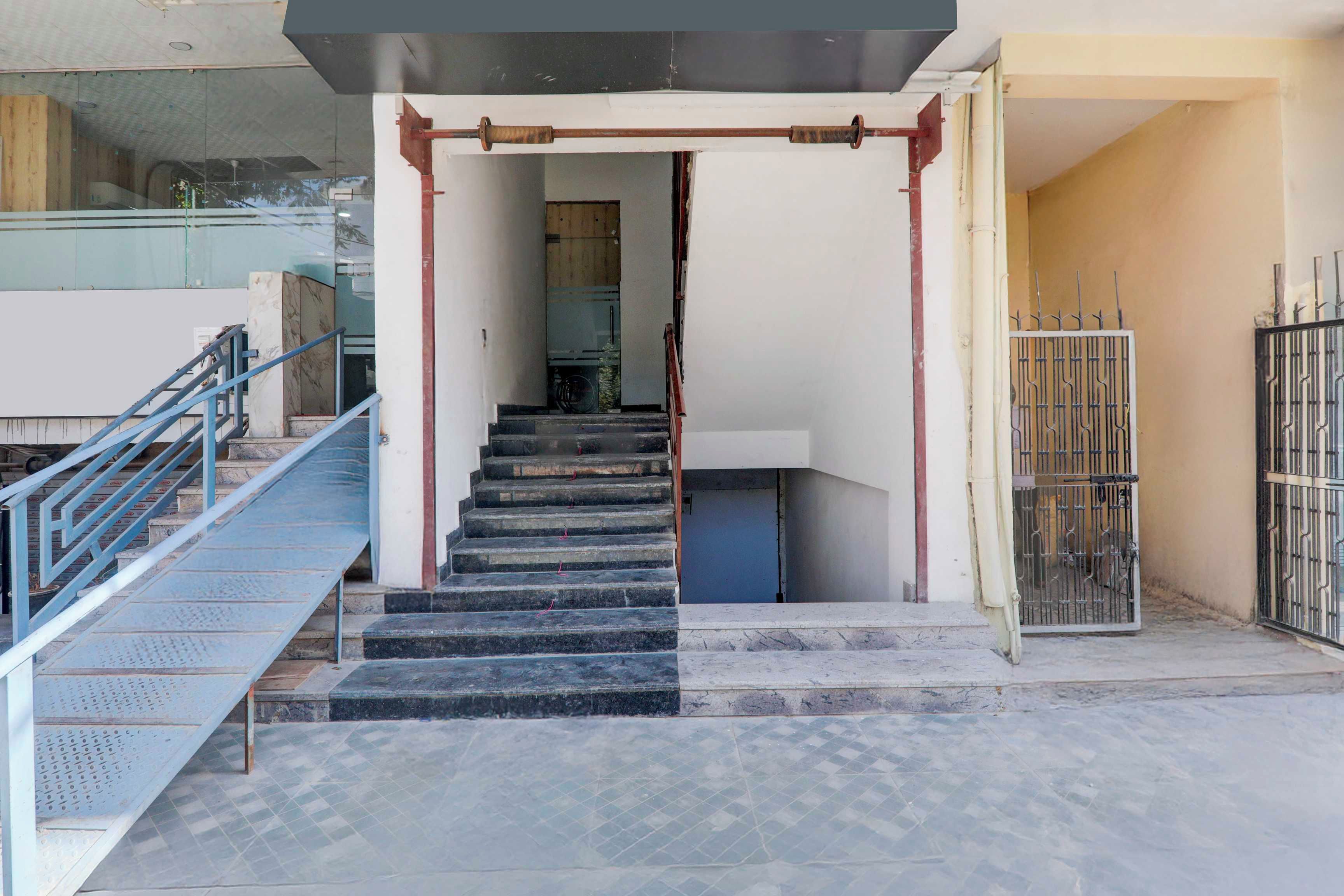 Escadaria com corrimão de metal que leva a um patamar, portão de metal e entrada de prédio.