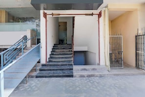 Escadaria com corrimão de metal que leva a um patamar, portão de metal e entrada de prédio.