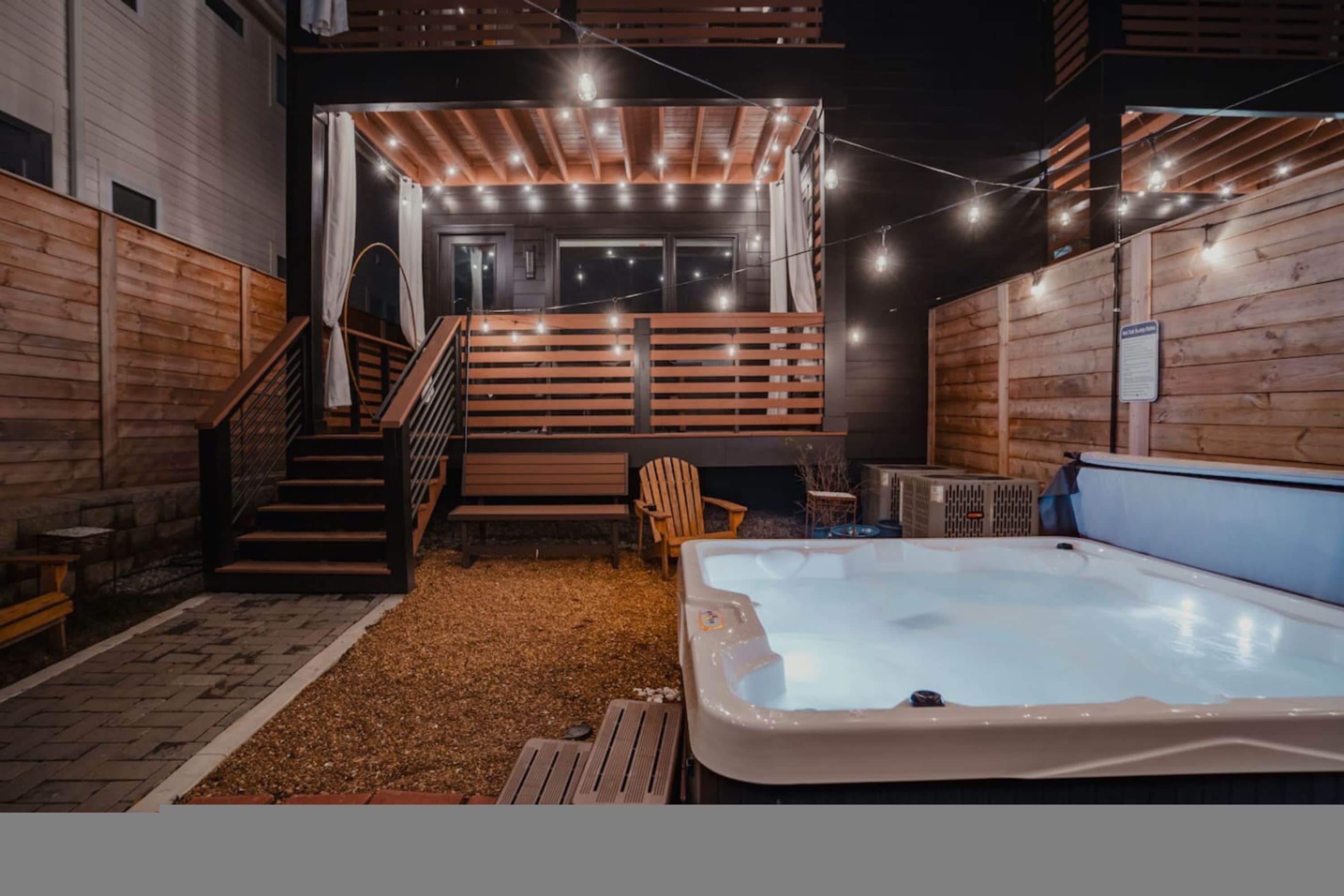 Uma banheira de hidromassagem em uma cabana de madeira, com uma escada que leva a um mezanino, cercada por luzes de corda.