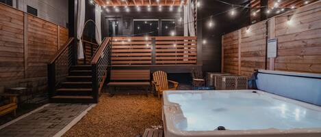 Uma banheira de hidromassagem em uma cabana de madeira, com uma escada que leva a um mezanino, cercada por luzes de corda.