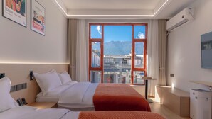 Quarto de hotel com uma janela grande, uma cama, uma escrivaninha e uma cadeira.