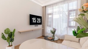 Uma sala de estar moderna com televisão de tela plana mostrando a hora, um sofá, uma mesa de centro e um vaso com planta.