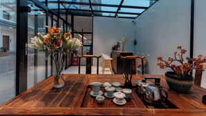 Mesa de madeira com jogos de chá e um vaso de flores em um interior moderno com paredes de vidro.