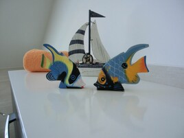 Dois objetos em formato de peixe sobre uma superfície branca, com um modelo de veleiro ao fundo.