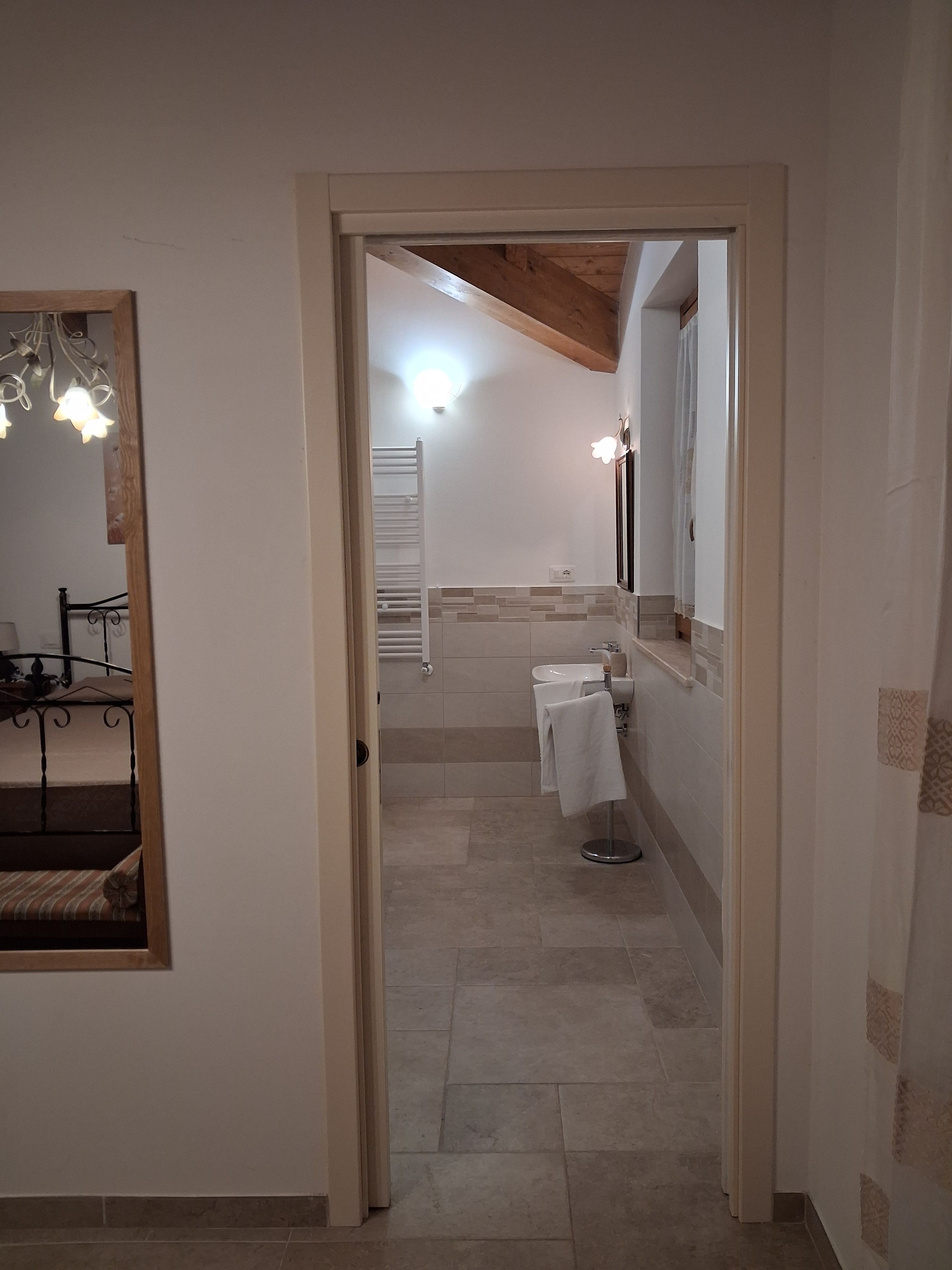 Corredor que leva a um banheiro com pia branca, porta-toalhas e espelho.