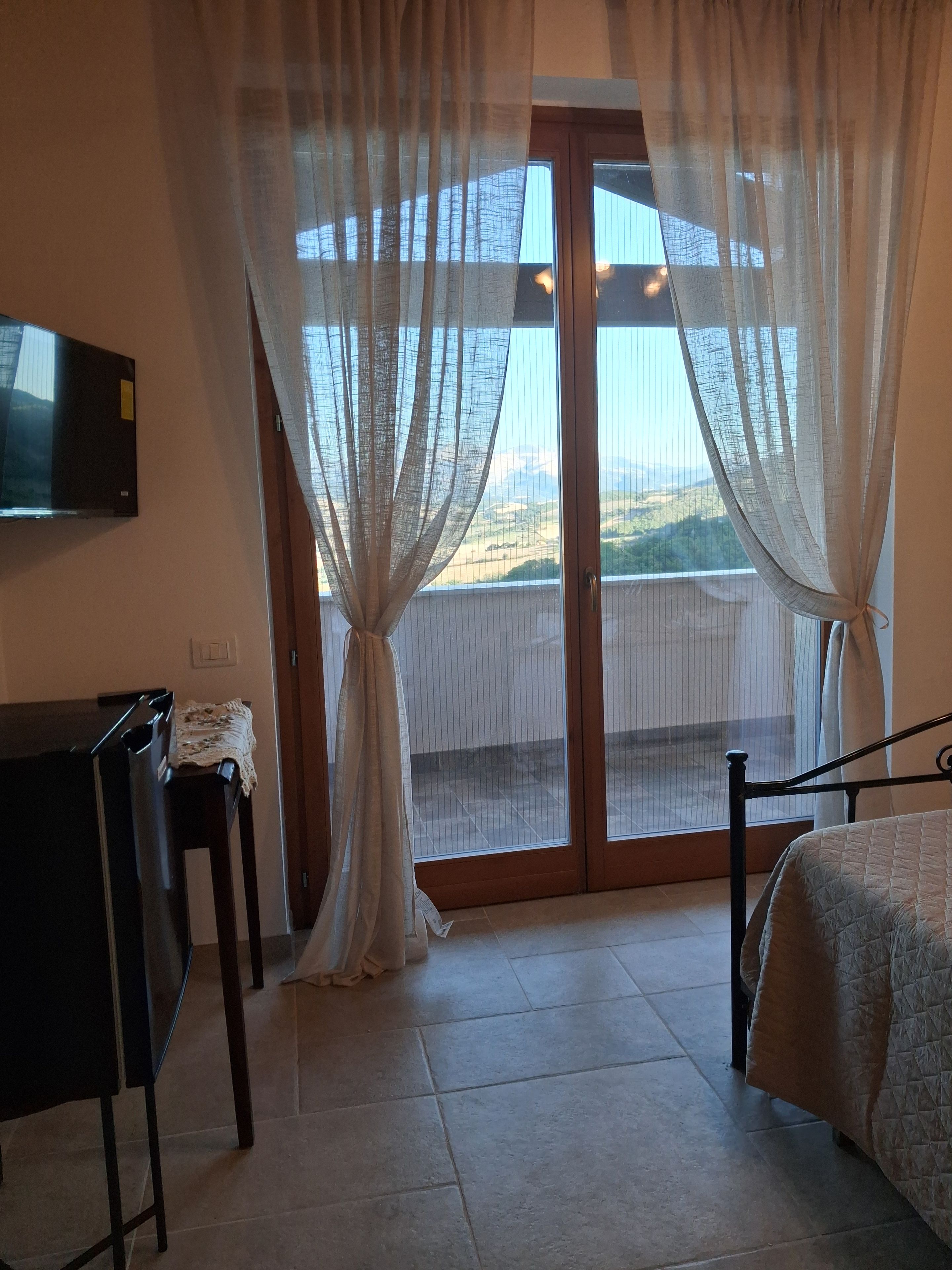 Quarto de hotel com cama, escrivaninha e televisão na parede.