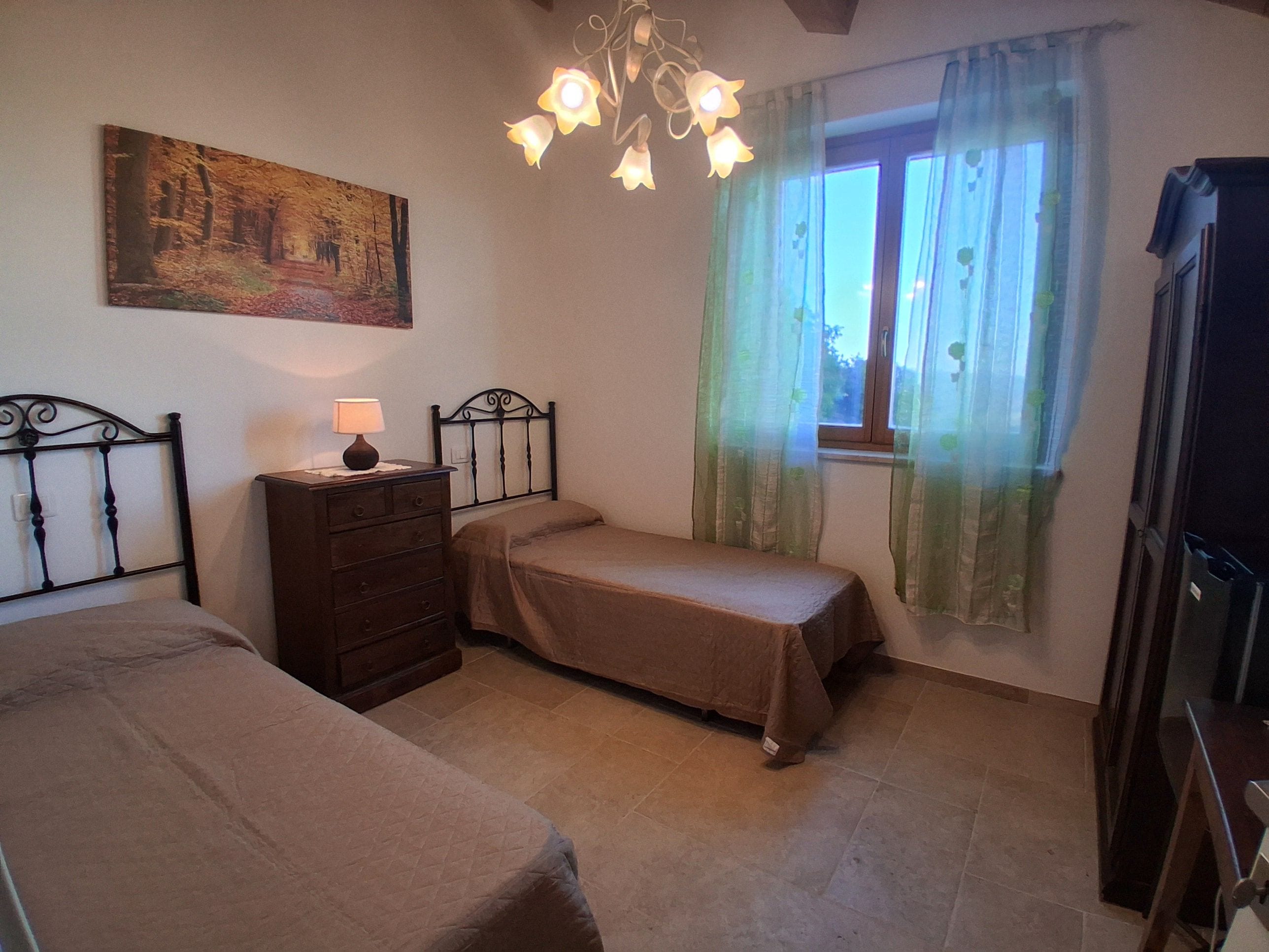 Quarto com duas camas, cômoda, luminária, pintura na parede e janela com cortinas.