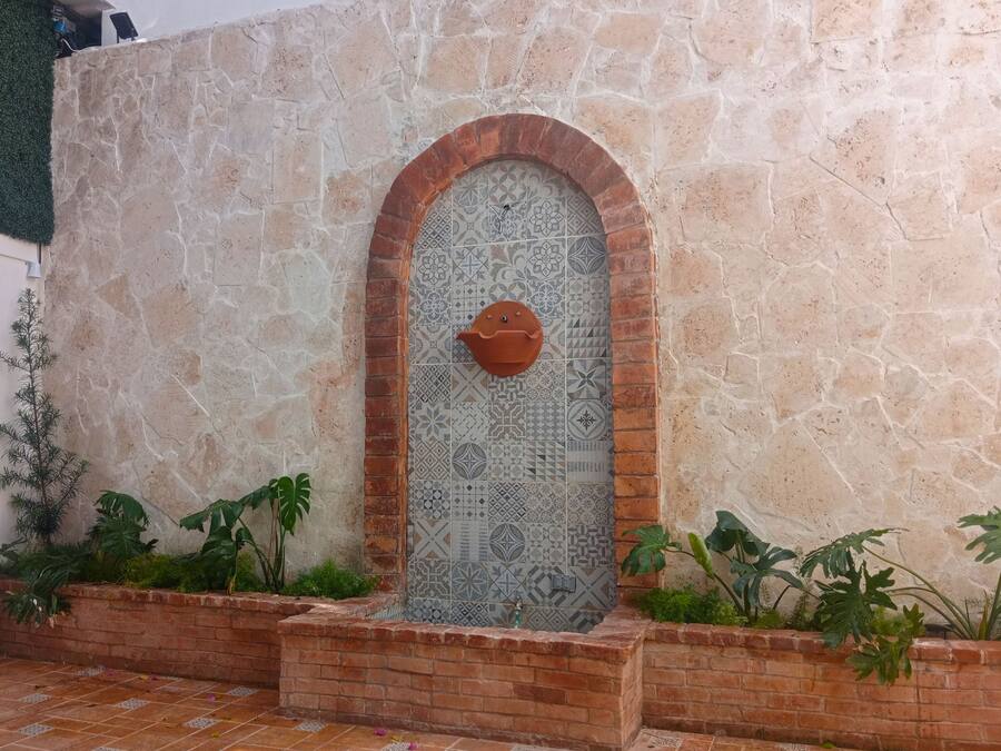 Parede de pedra com porta azulejada, detalhes em padrões geométricos e um vaso de terracota.