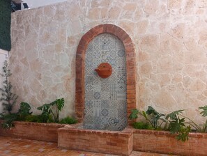 Parede de pedra com porta azulejada, detalhes em padrões geométricos e um vaso de terracota.