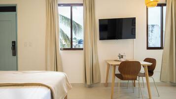 Quarto de hotel com cama, escrivaninha com duas cadeiras, televisão de tela plana e janela com cortinas.