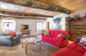 Uma sala de estar aconchegante com teto de madeira, um sofá vermelho, um sofá cinza e uma televisão sobre um suporte de madeira.