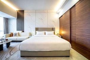 Quarto de hotel moderno com uma cama grande, um sofá, uma mesinha de cabeceira e uma luminária.
