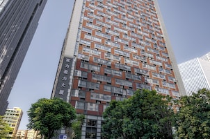 Um edifício alto com fachada padronizada, cercado por árvores e outros edifícios.