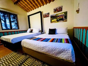 Quarto com duas camas, janela com vista para árvores e arte nas paredes retratando veículos.