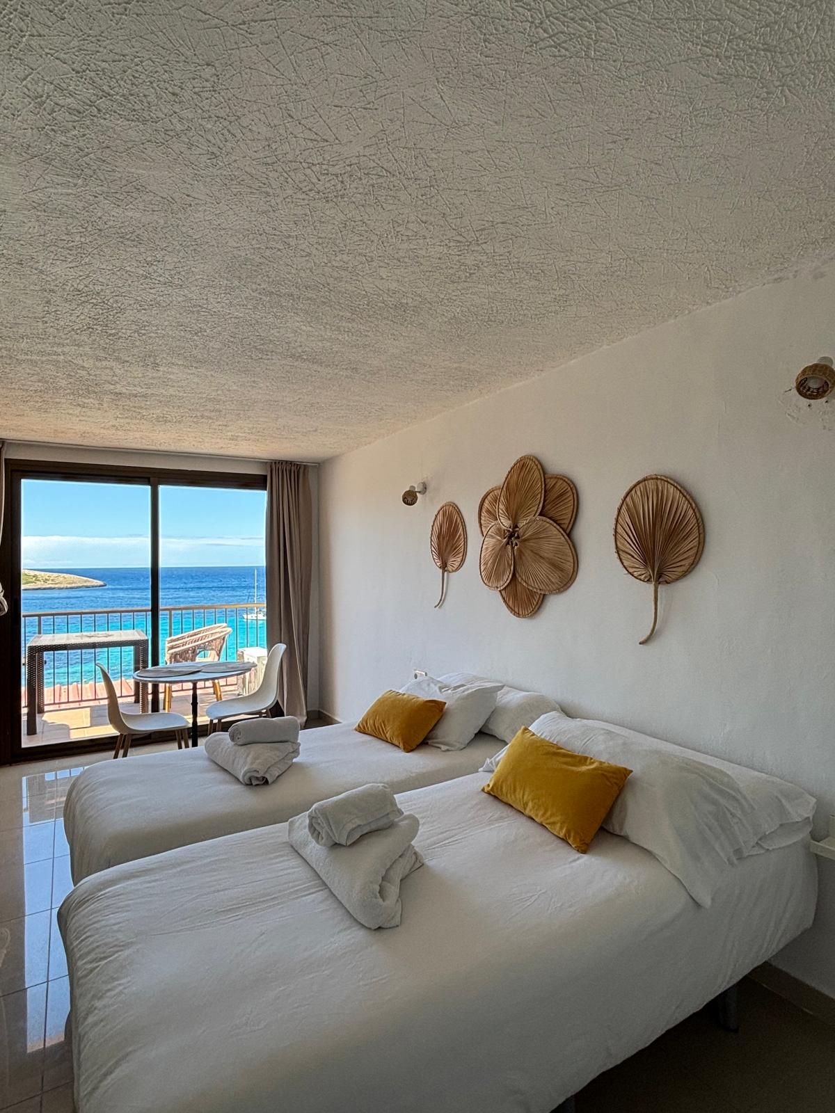 Quarto de hotel com duas camas, vista para o mar e varanda com mobiliário de exterior.